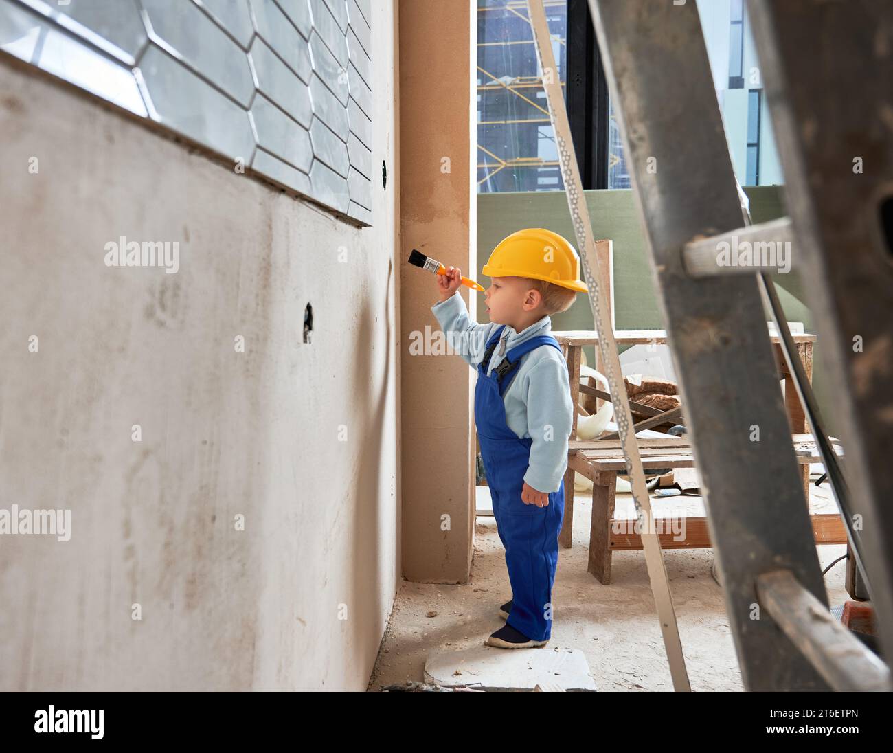 Side view of little boy construction worker painting wall with brush in ...