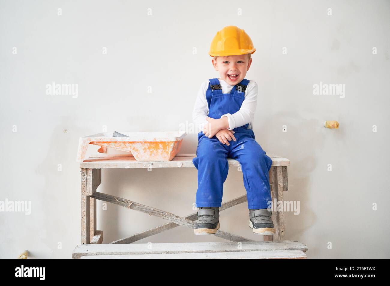 Cute kid construction worker sitting on wooden table against white wall ...