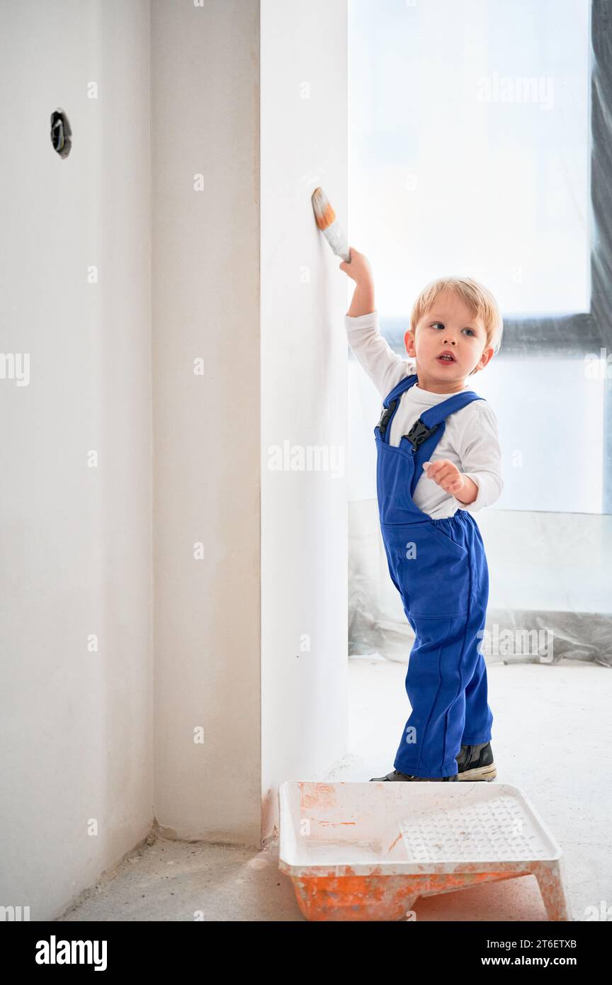 Child construction worker painting wall with paint brush in living room ...