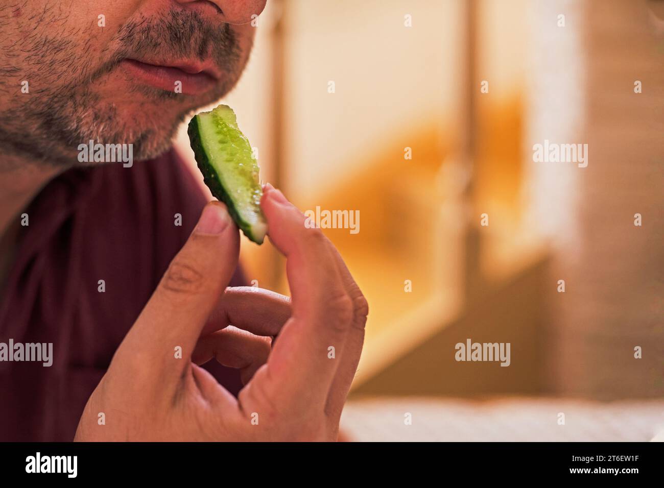man holds a piece of fresh cucumber in his hands and puts it in his ...