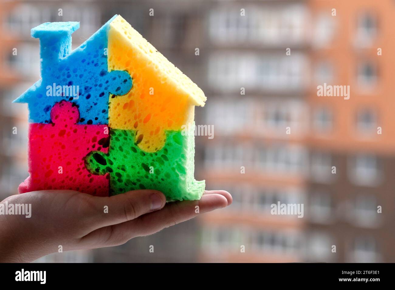 Hands holding a house against the background of a multi-storey building ...