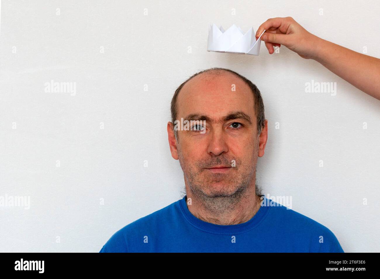 man and a white paper crown. The man is offered a crown. Hands hold the ...