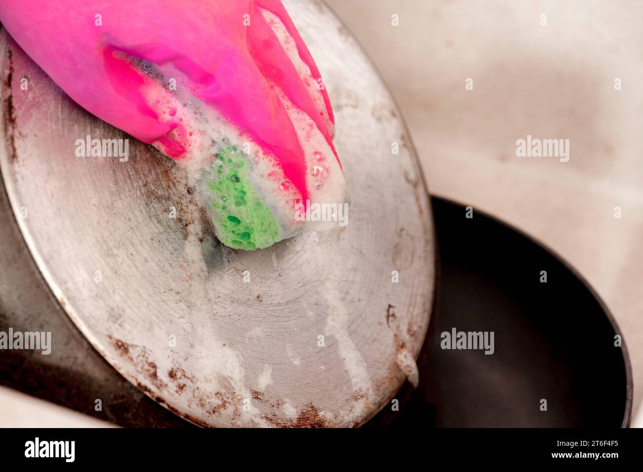 Cleaning a dirty frying pan with a kitchen sponge in the glove. Female ...