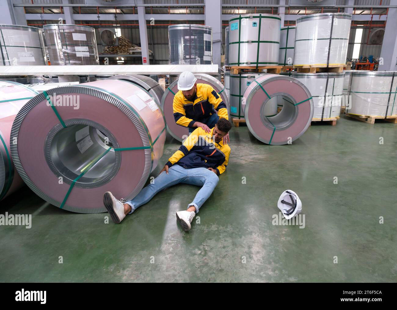 Two factory workers are seated on the floor, one assisting the other ...