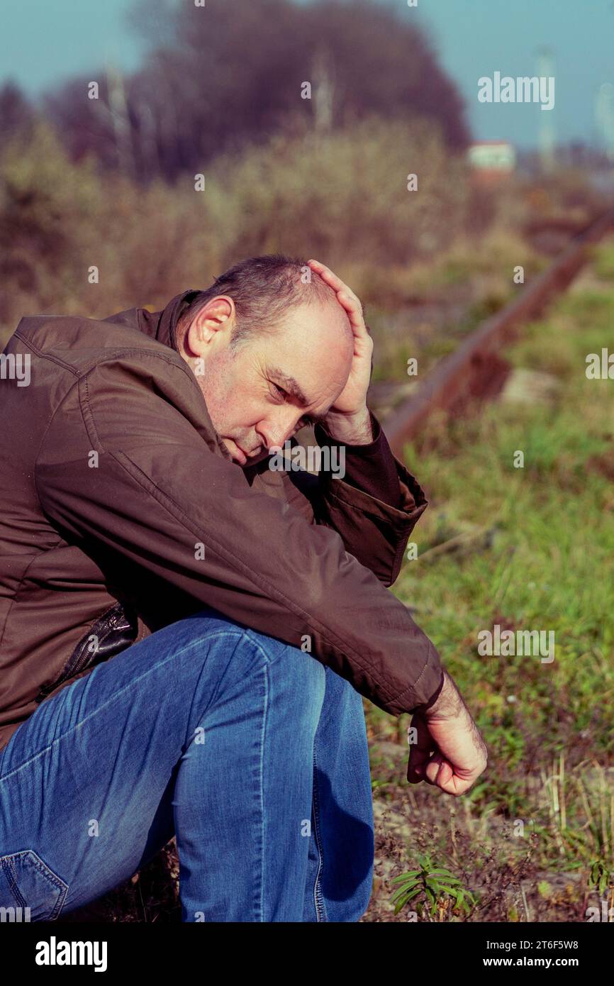 The thoughtful man sits on rails. The upset person in a stress. Concept ...