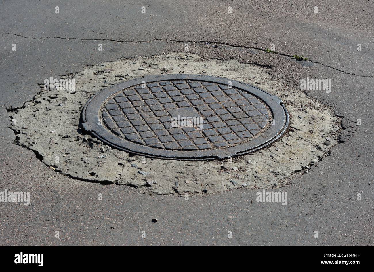 Close up on metal manhole cover on asphalt road with concrete repair ...