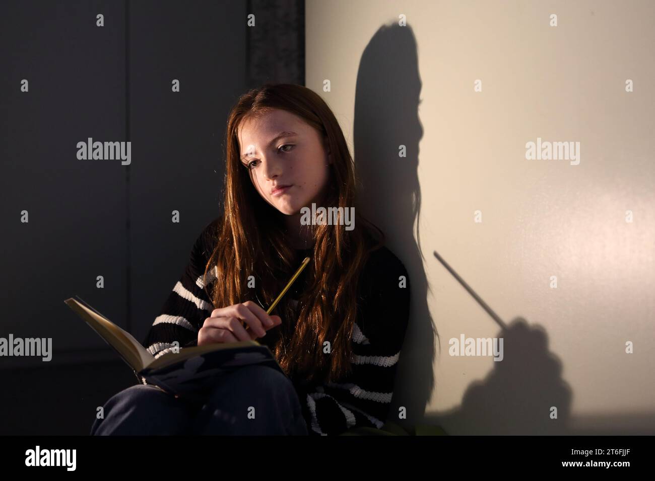 Teenage girl thinking and making notes with a pencil in a notebook ...