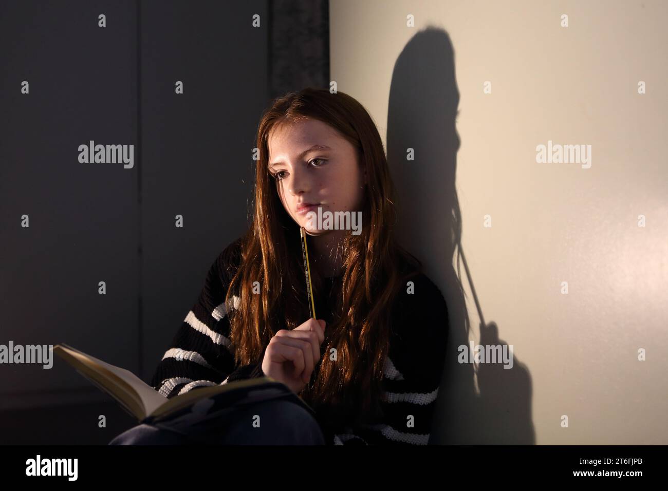 Teenage girl making notes with a pencil in a notebook, thinking about ...