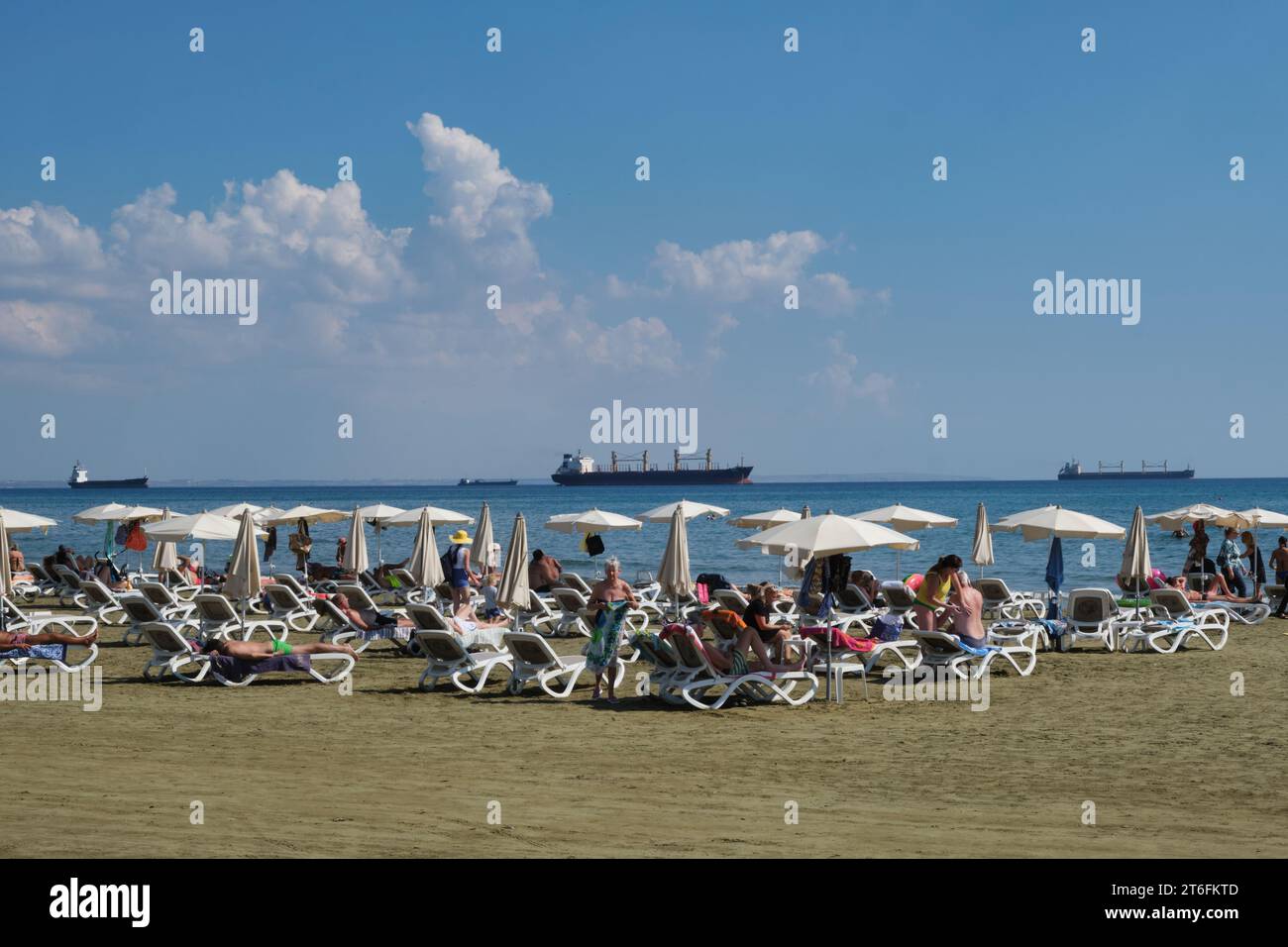 Container ship leave port as sunbathers enjoy late summer sun on Larnaca beach in Cyprus Stock ...