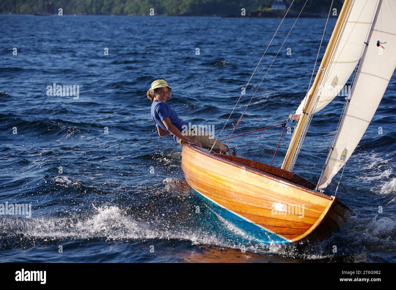 A teenaged boy happily sails a classic wooden sailing dinghy on a ...