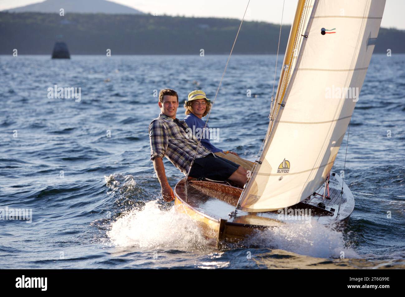 Two teenaged boys sail on a classic wooden sailing dinghy, on a ...