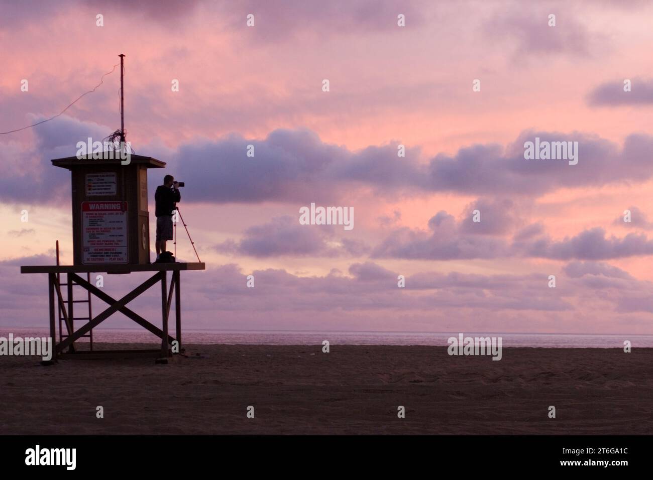 A photographer takes a photo of the sunset from a lifeguard stand at ...