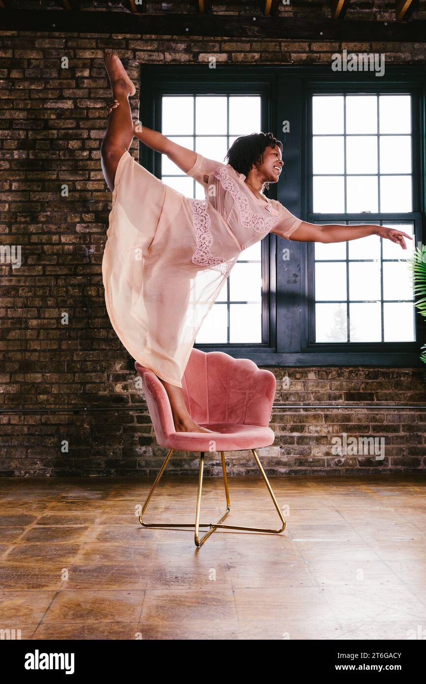 Black female dancer in standing split pose on chair in dress Stock ...