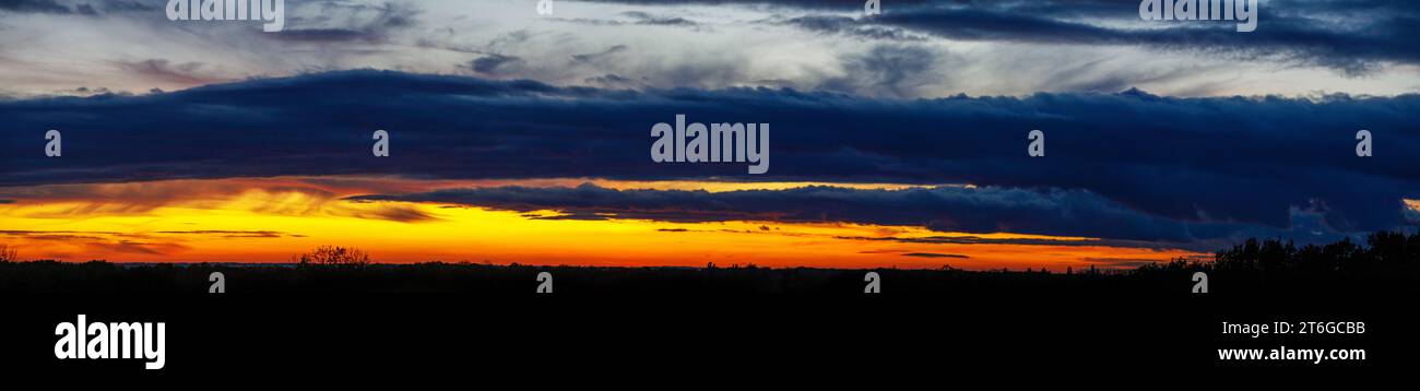 Panoramic sunset sky with heavy dark blue clouds and orange line of sun ...