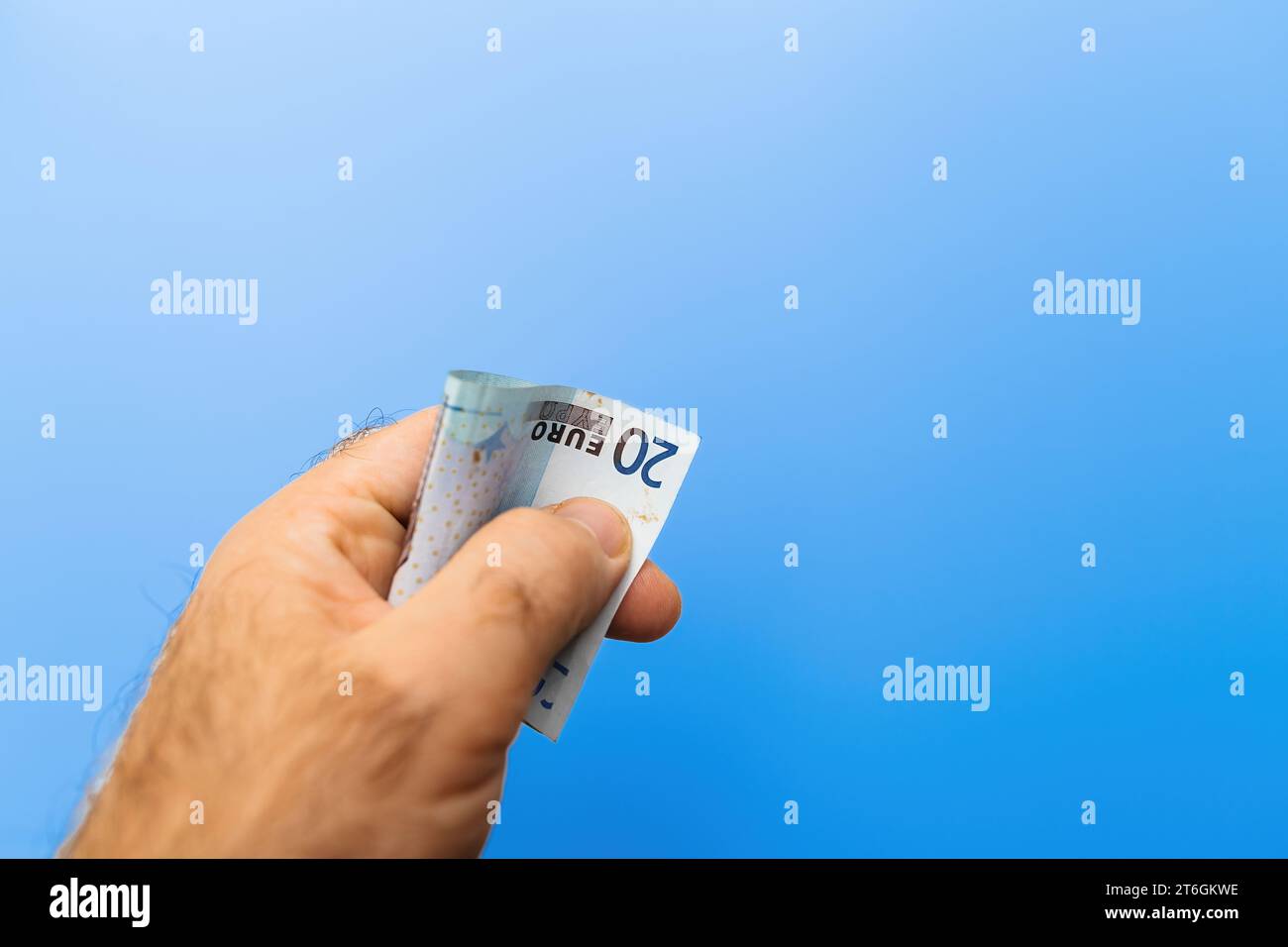 A close-up image capturing a hand holding out a folded 20 Euro banknote ...