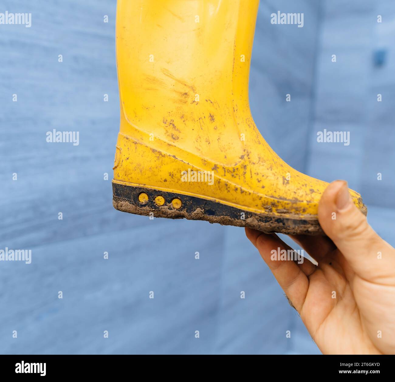 A male hand grips a pair of child's yellow rubber boots, soiled with ...