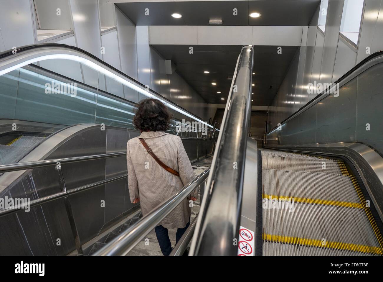Woman from behind descending staircase in between escalators to train ...