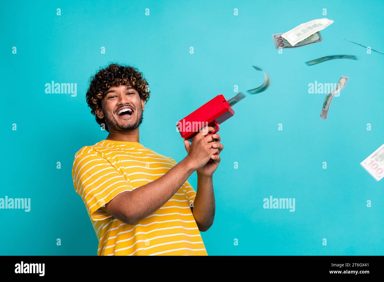 Photo of overjoyed successful guy hold money gun shooting flying dollar ...