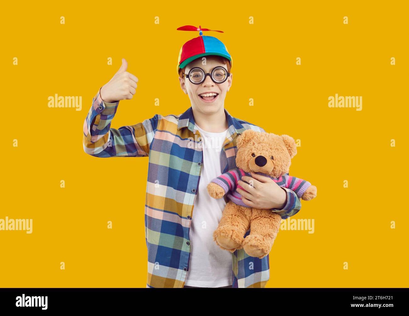 Funny boy in propeller cap and glasses holding teddy bear, giving ...