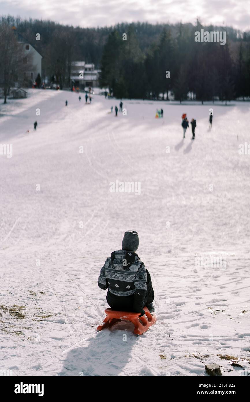 Girl sits on a sledge on a hill and looks at the rink with sleigh ...