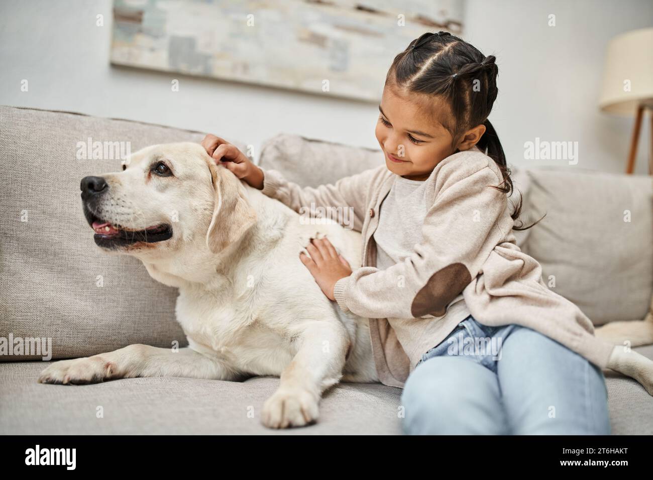 happy kid sitting on sofa and cuddling cute labrador in modern living ...