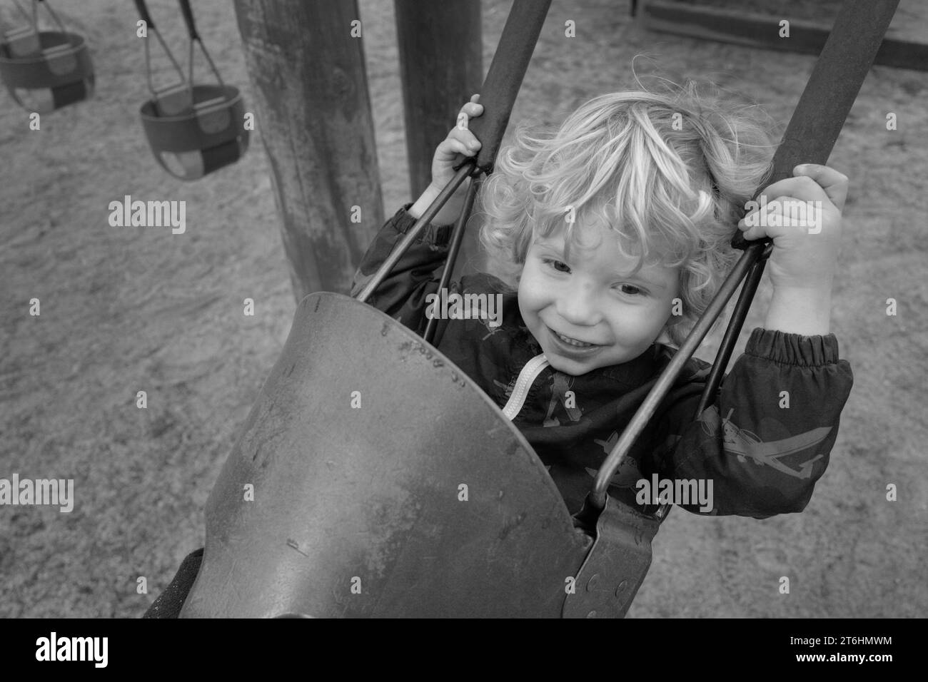 Two-year-old boy enjoys being pushed on a swing at a local playground ...