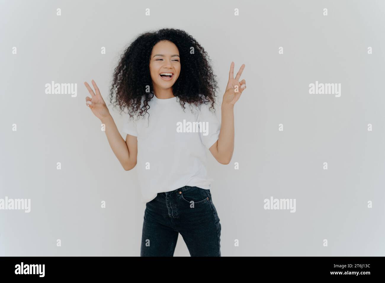 Exuberant young woman with curly hair making peace signs with both ...