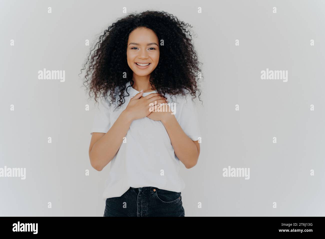 Grateful young lady with curly hair, hands on heart, expressing genuine ...