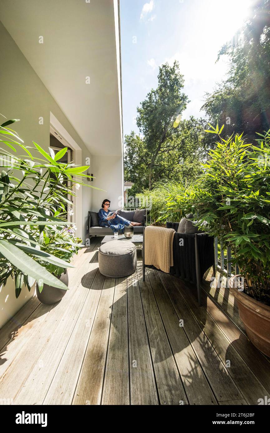 Woman sitting on the balcony with modern lounge furniture and reading a ...