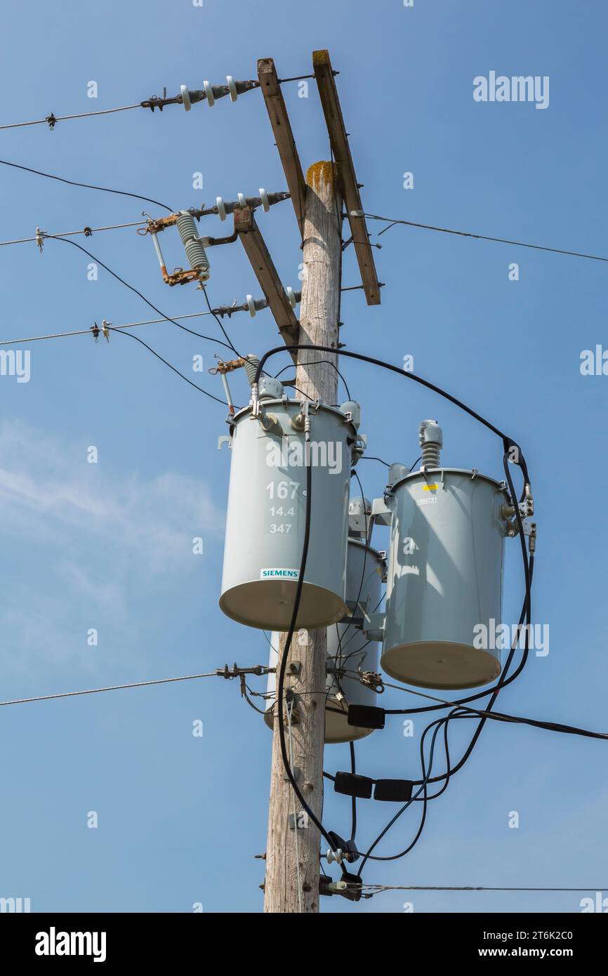 Electricity transformers and transmission cables plus distribution wires mounted on wooden pole ...