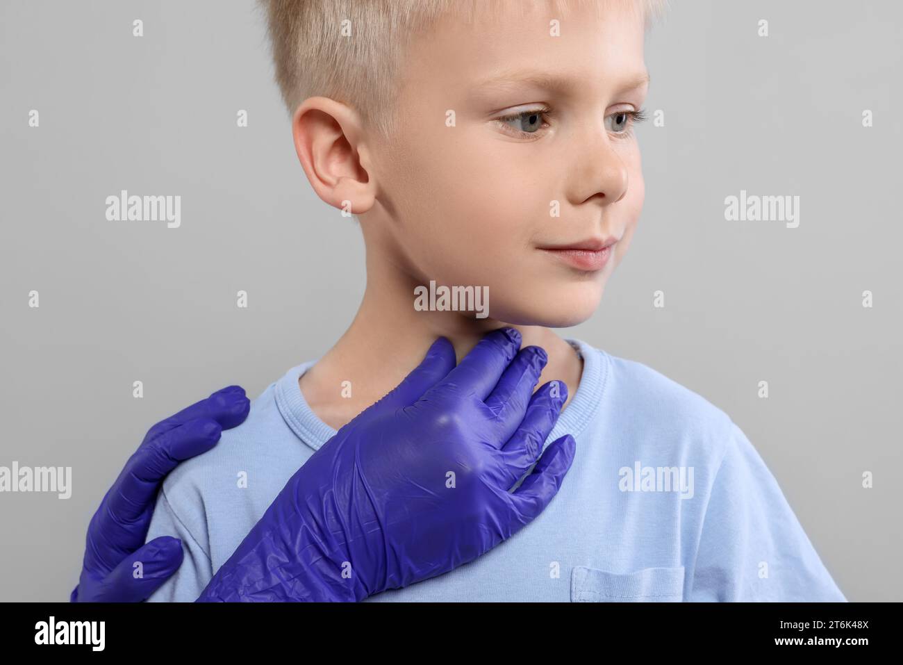 Endocrinologist examining boy's thyroid gland on light grey background ...