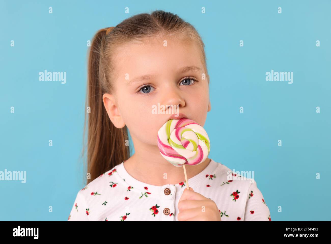 Cute little girl licking colorful lollipop swirl on light blue ...
