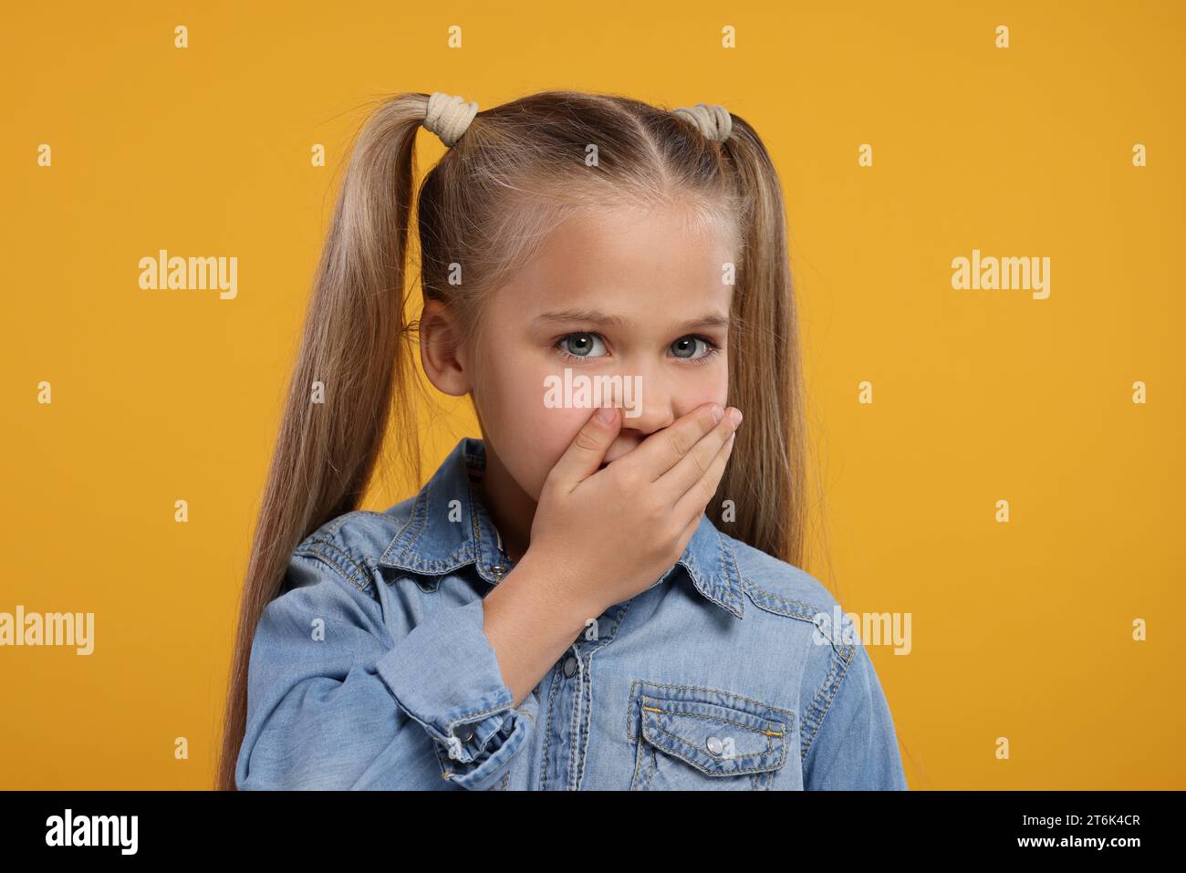 Embarrassed little girl covering her mouth with hand on orange ...