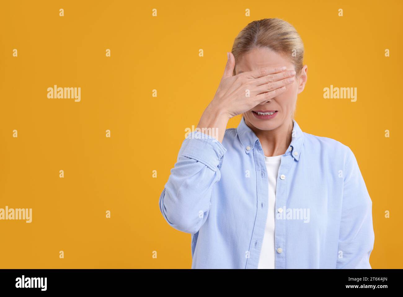 Embarrassed woman covering eyes with hands on orange background. Space ...