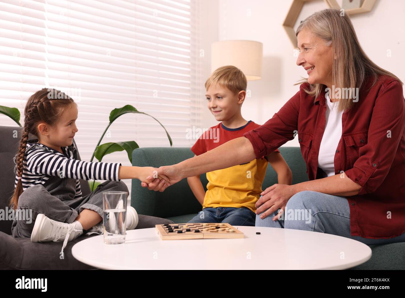 Family playing checkers at coffee table in room. Grandmother shaking hands with her nephew after ...