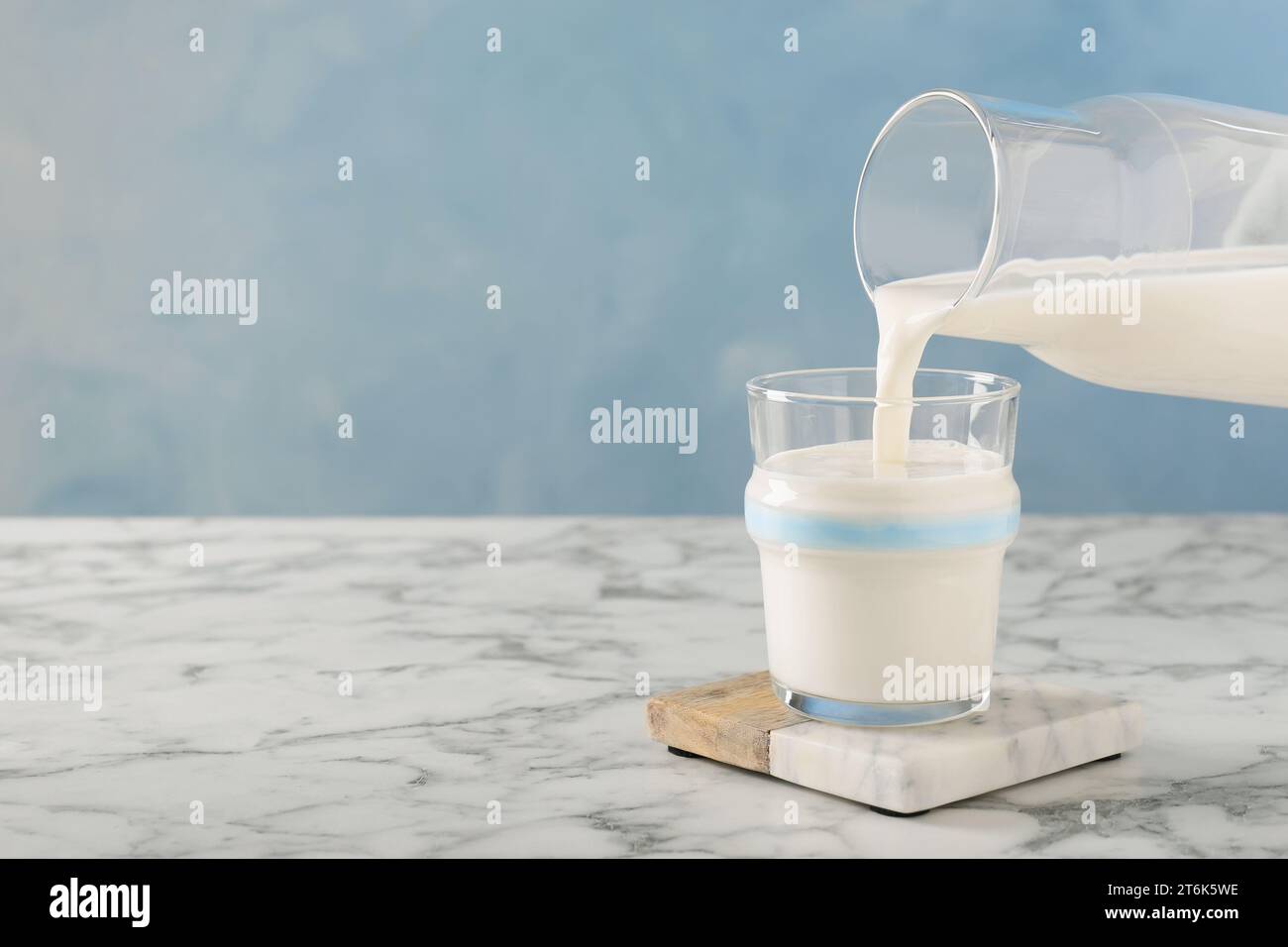 Pouring fresh milk into glass on white marble table, space for text ...