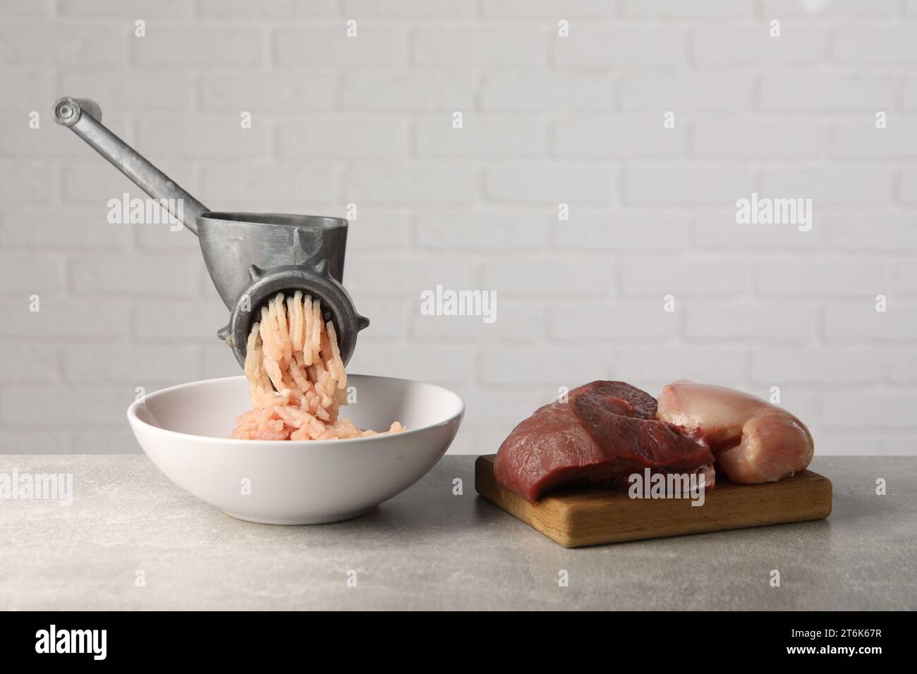 Metal meat grinder with mince, raw chicken and beef on grey table near ...