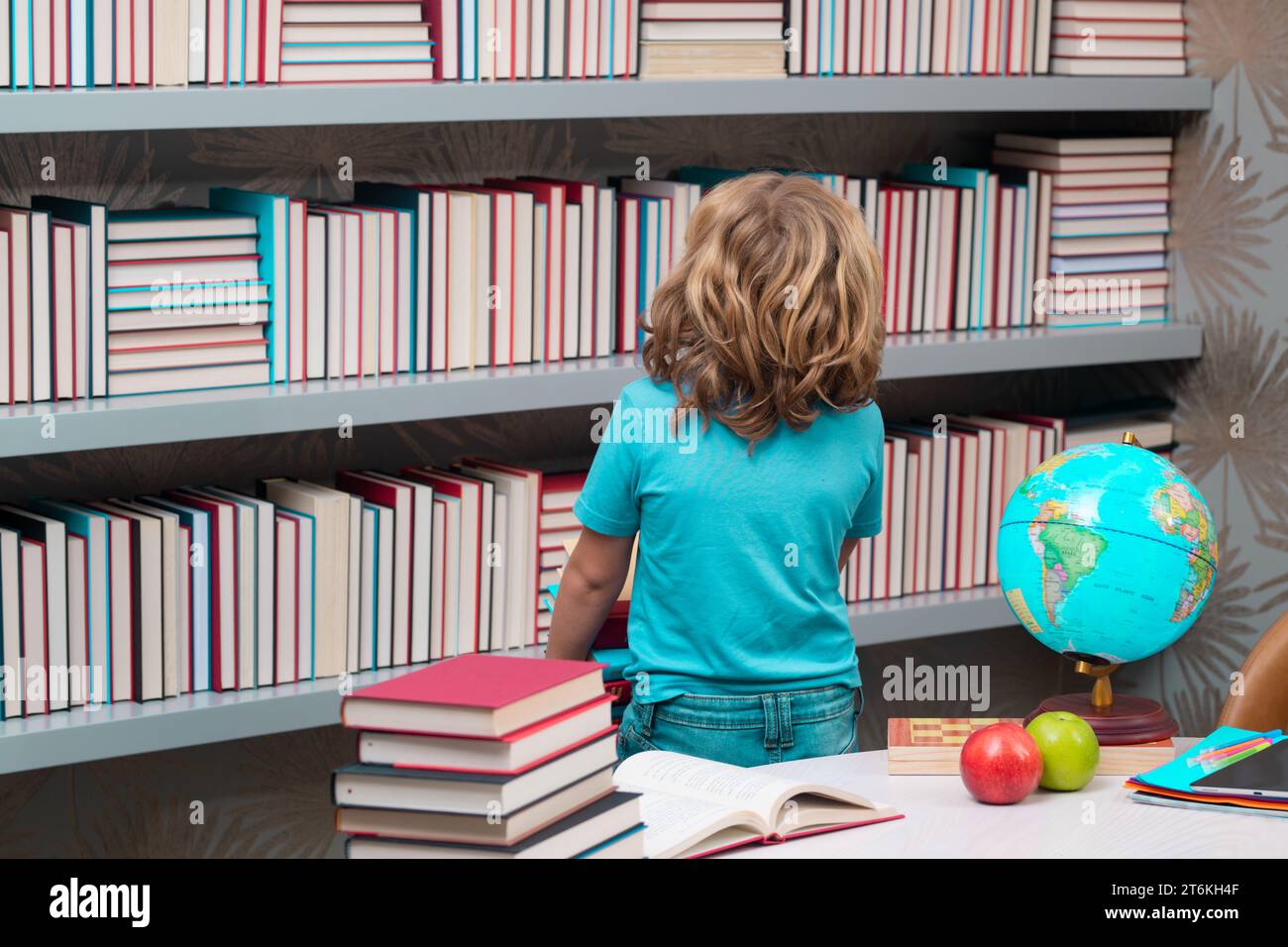 School boy with stack of books in library. Child from elementary school ...