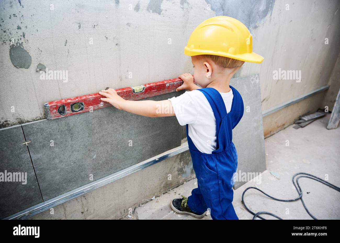 Child construction worker checking wall surface with spirit level tool ...
