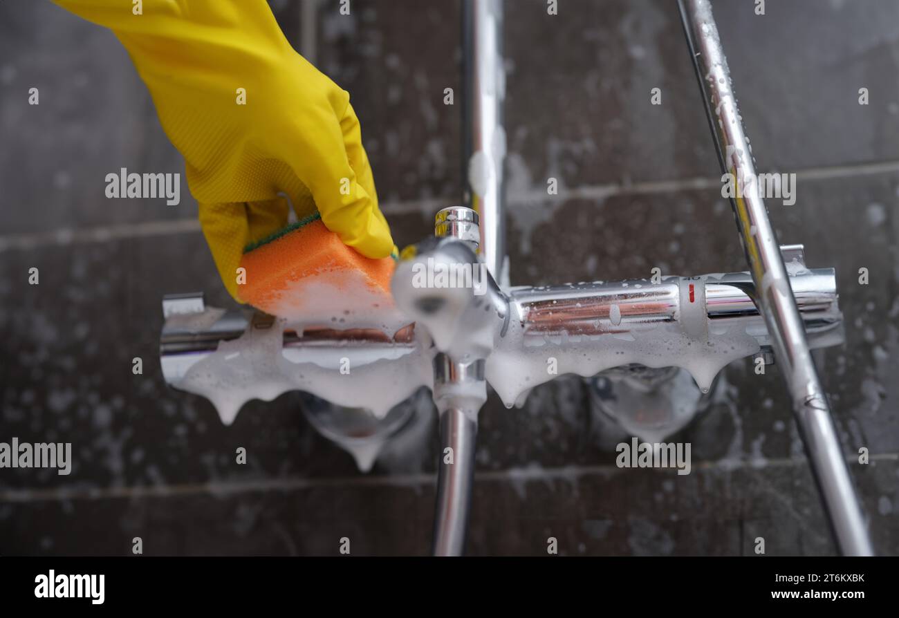 Cleaning lady in rubber glove washes faucet in bathroom with sponge ...