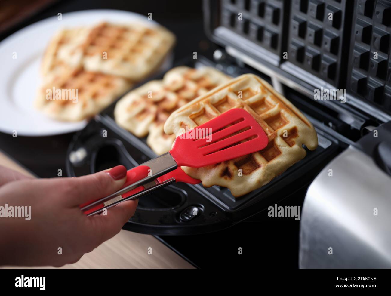 Female hands finishing making waffles on waffle iron in bakery Stock ...