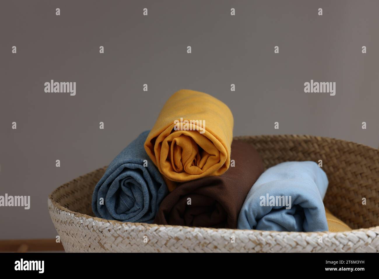 Different rolled shirts in basket against grey background. Organizing ...