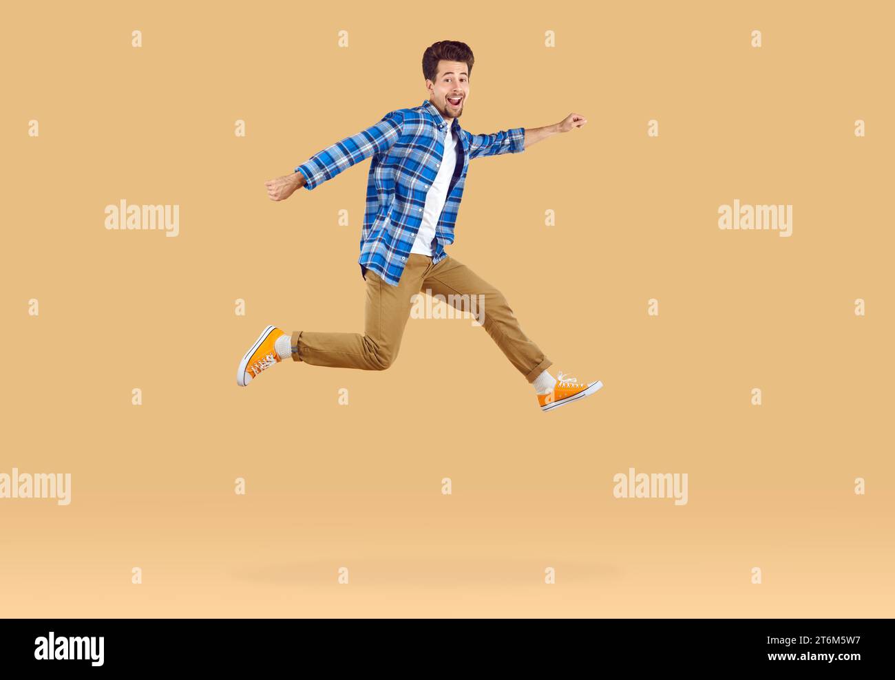 Handsome happy guy jumping high in air on beige background with copy ...