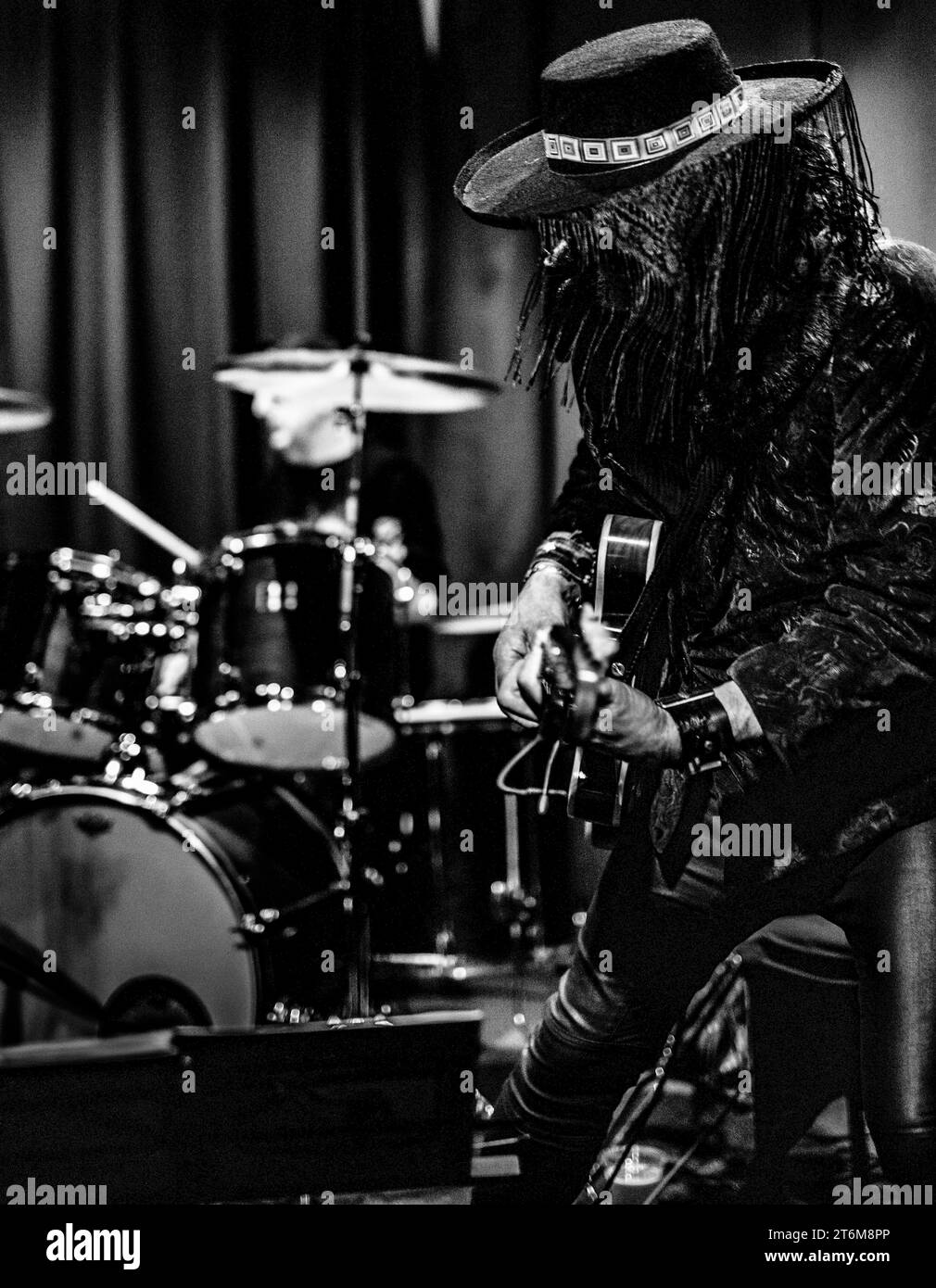 A male musician is strumming an acoustic guitar while seated on a stool ...