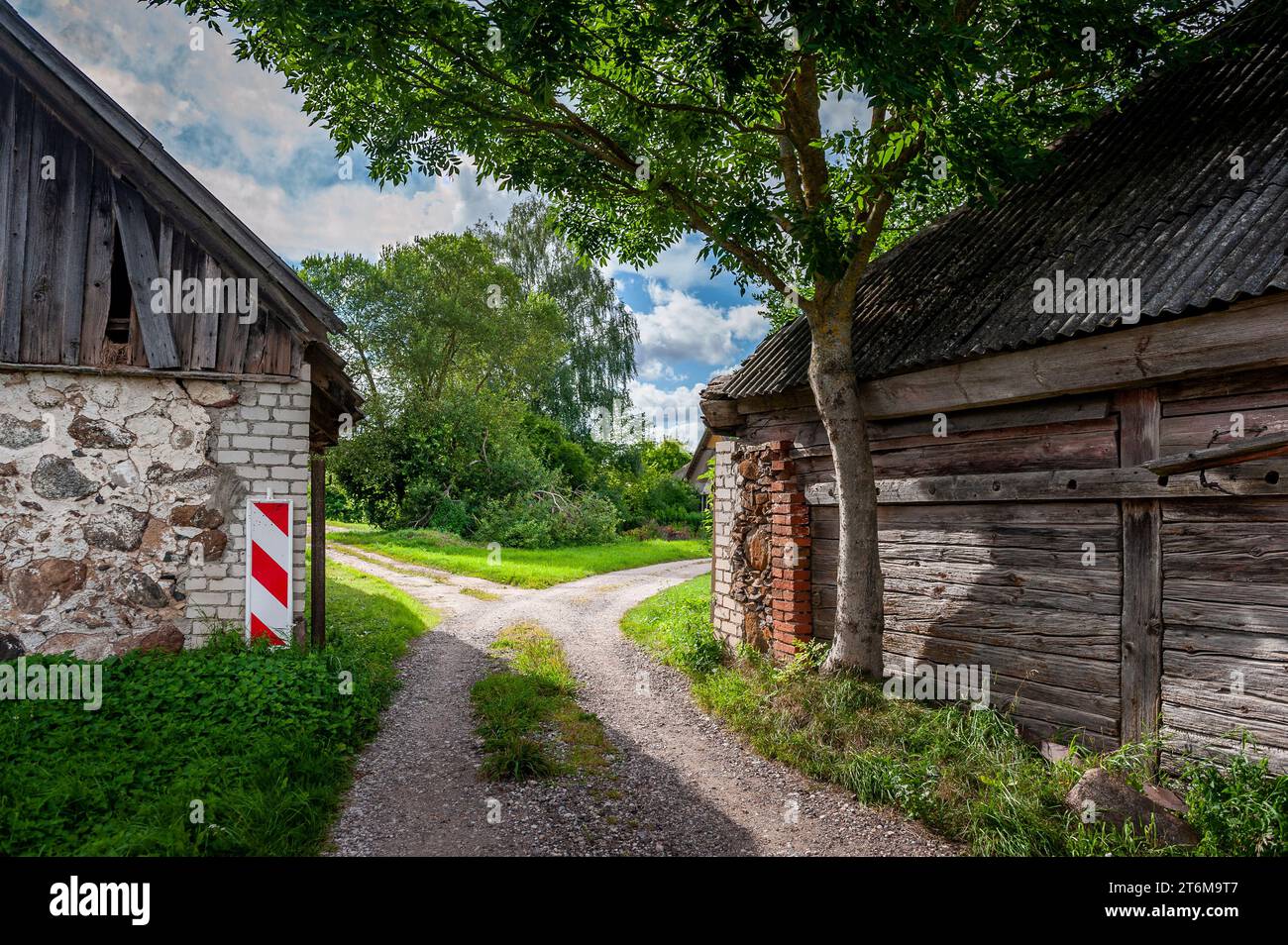 Rural road runs between two barns. A road junction and directional sign ...