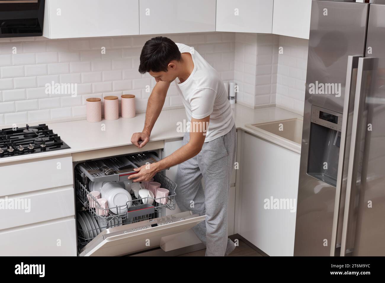 handsome positive man putting plates in dishwasher machine in the ...