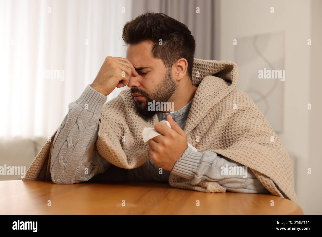 Sick man wrapped in blanket with tissue at wooden table indoors. Cold ...