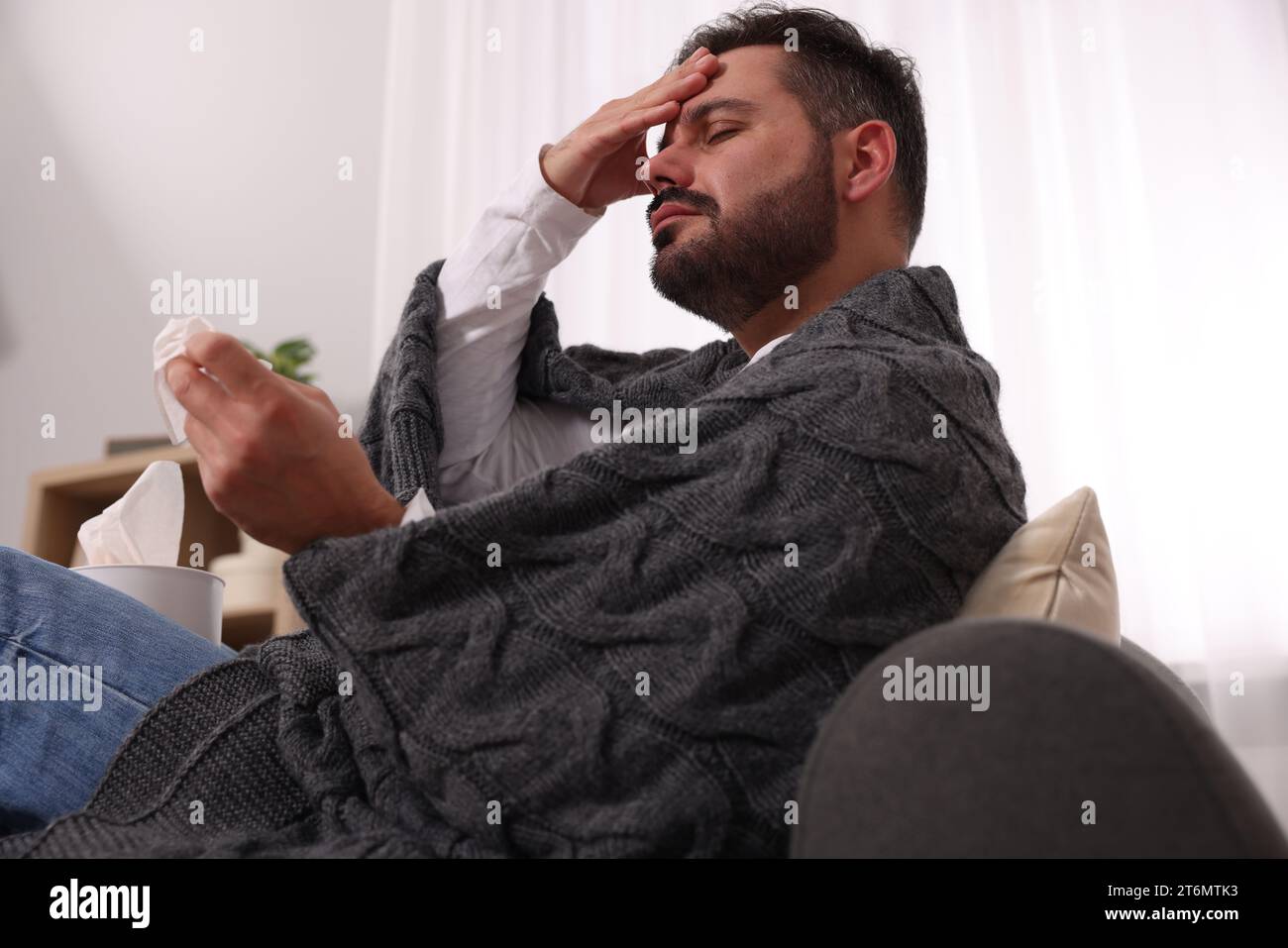 Sick man wrapped in blanket with tissue on sofa at home. Cold symptoms ...