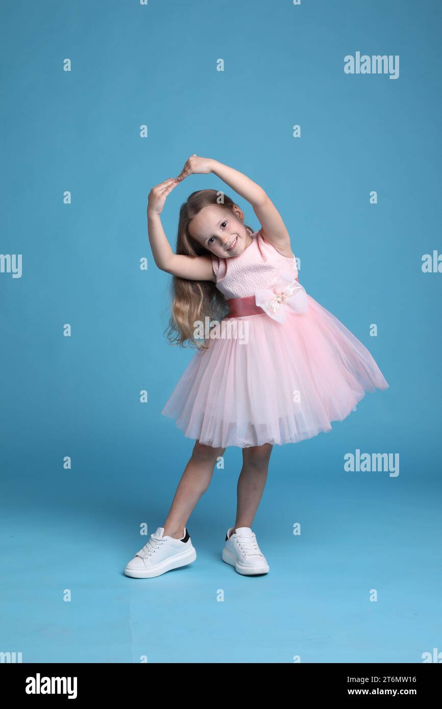 Cute little girl in beautiful dress dancing on light blue background ...