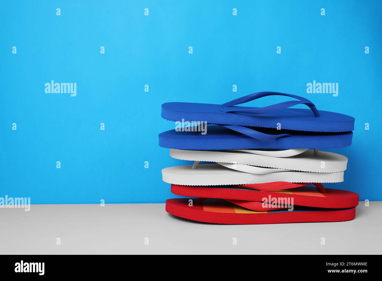 Stack of different flip flops on white table against light blue ...